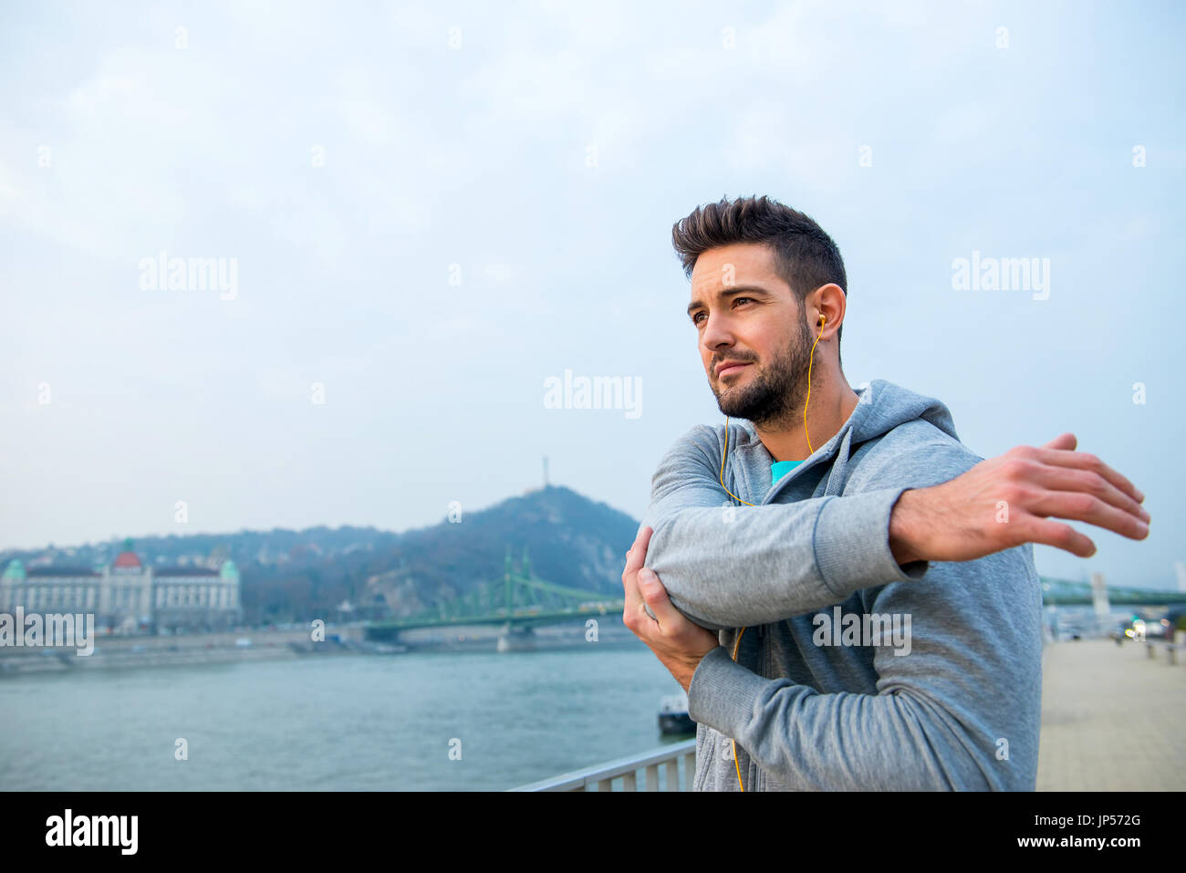 A handsome young man standing and stretching his arm at the riverside ...