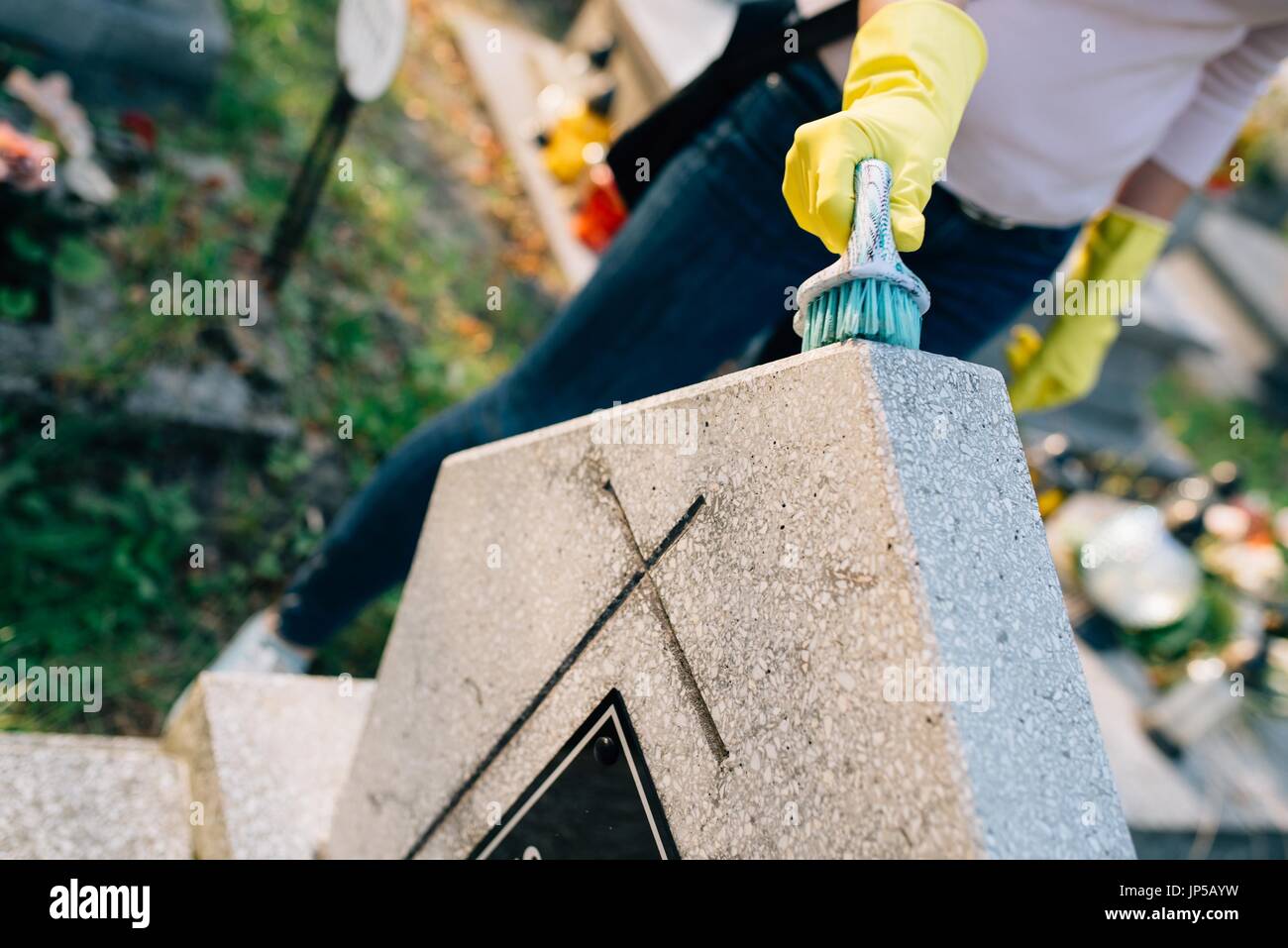 A woman cleans the grave. Washing tombstone with brush. Preparations ...