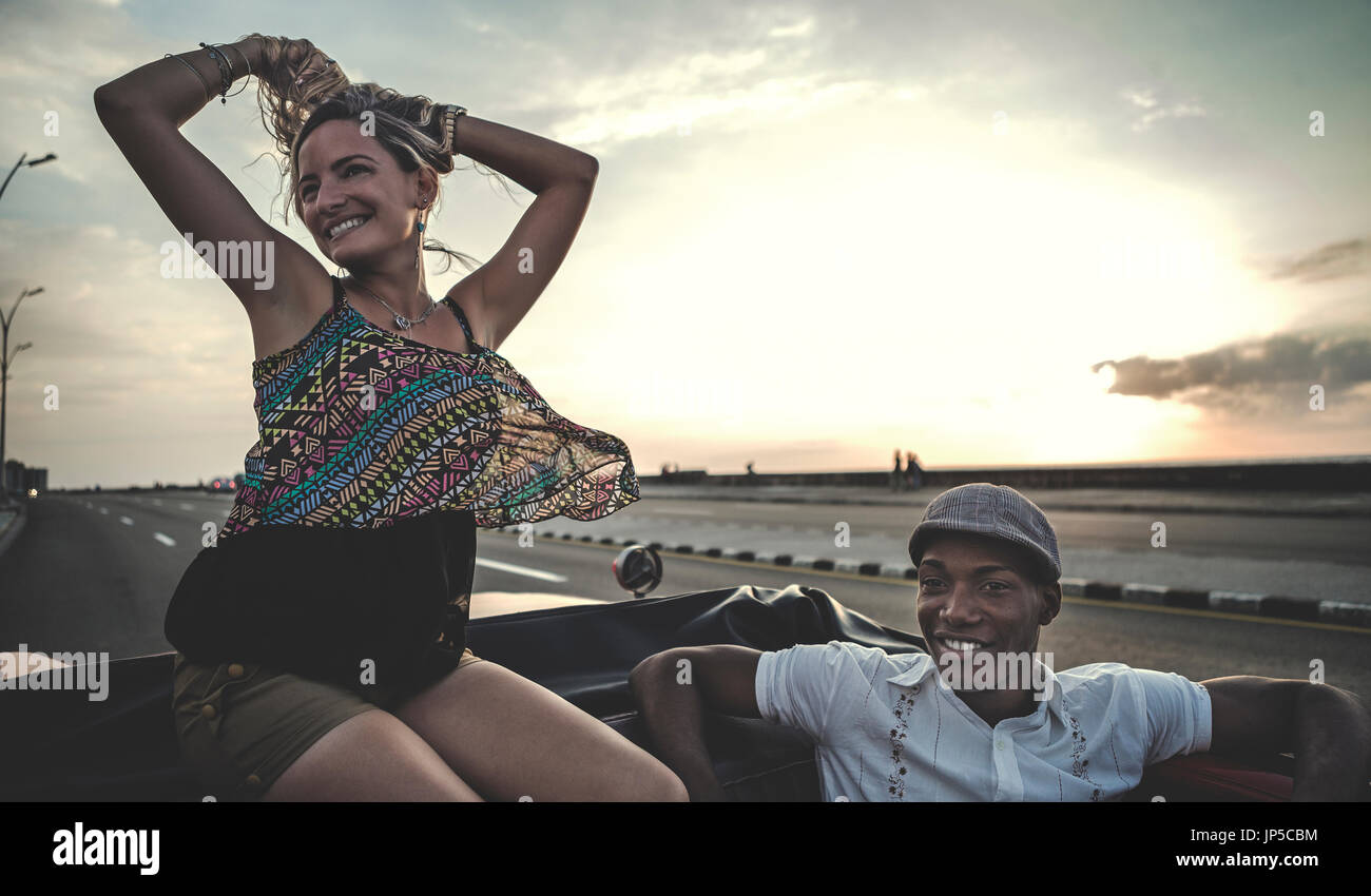 Two people riding through a city in an open convertible classic car ...