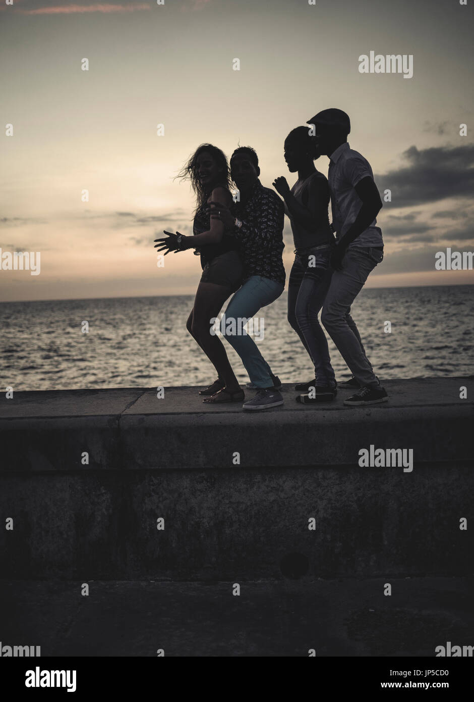 Four people dancing in a line on a sea wall next to the ocean Stock ...