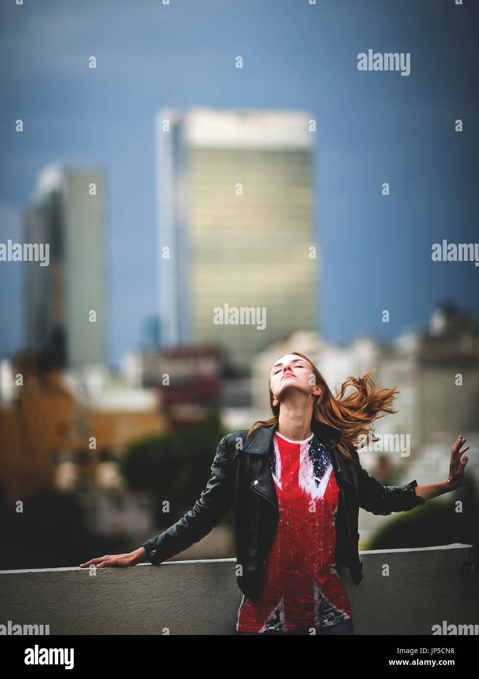 A woman standing and dancing on a city rooftop, with tall buildings ...