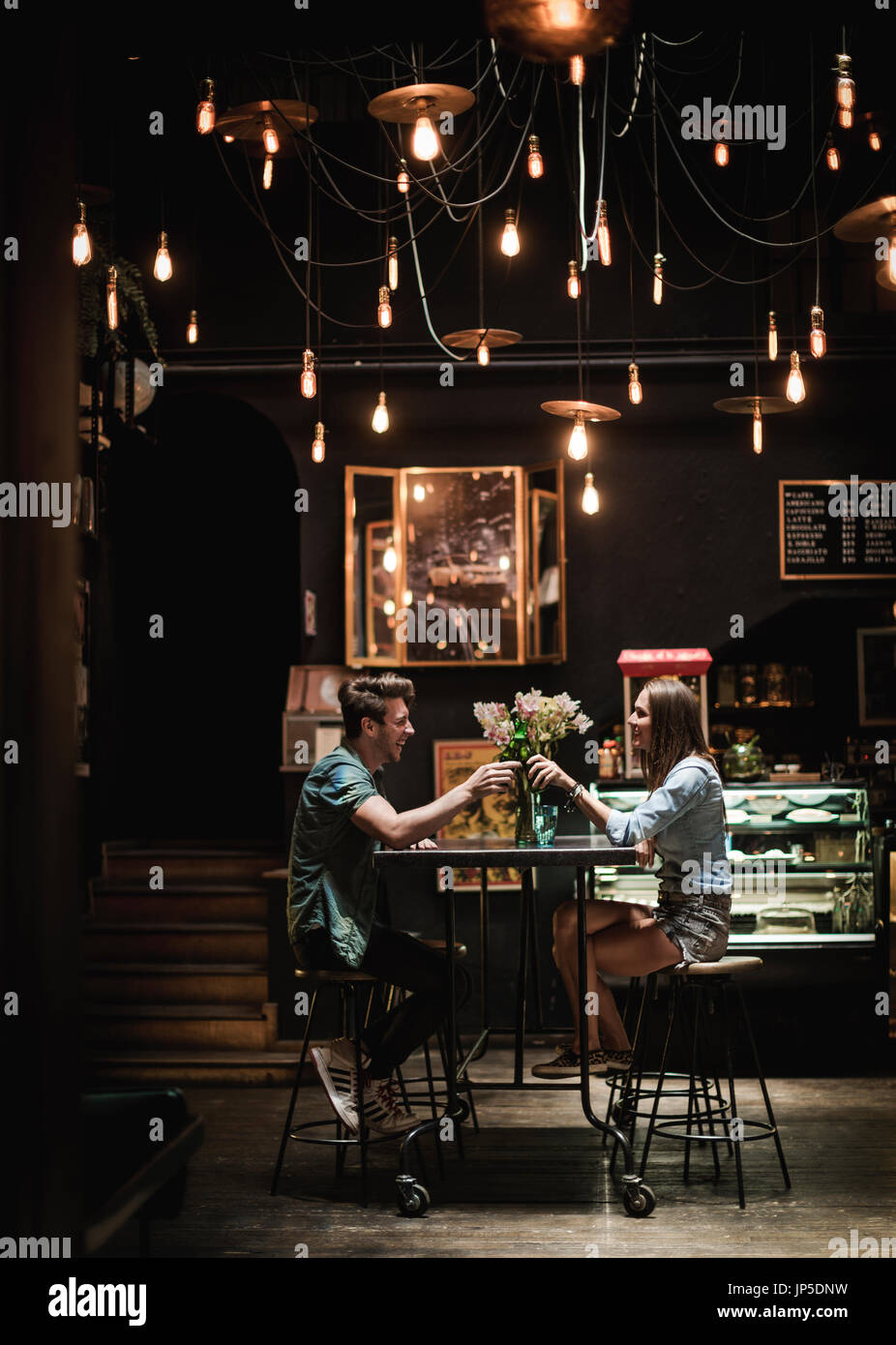 Two young people sitting at a table in a bar under a large light ...