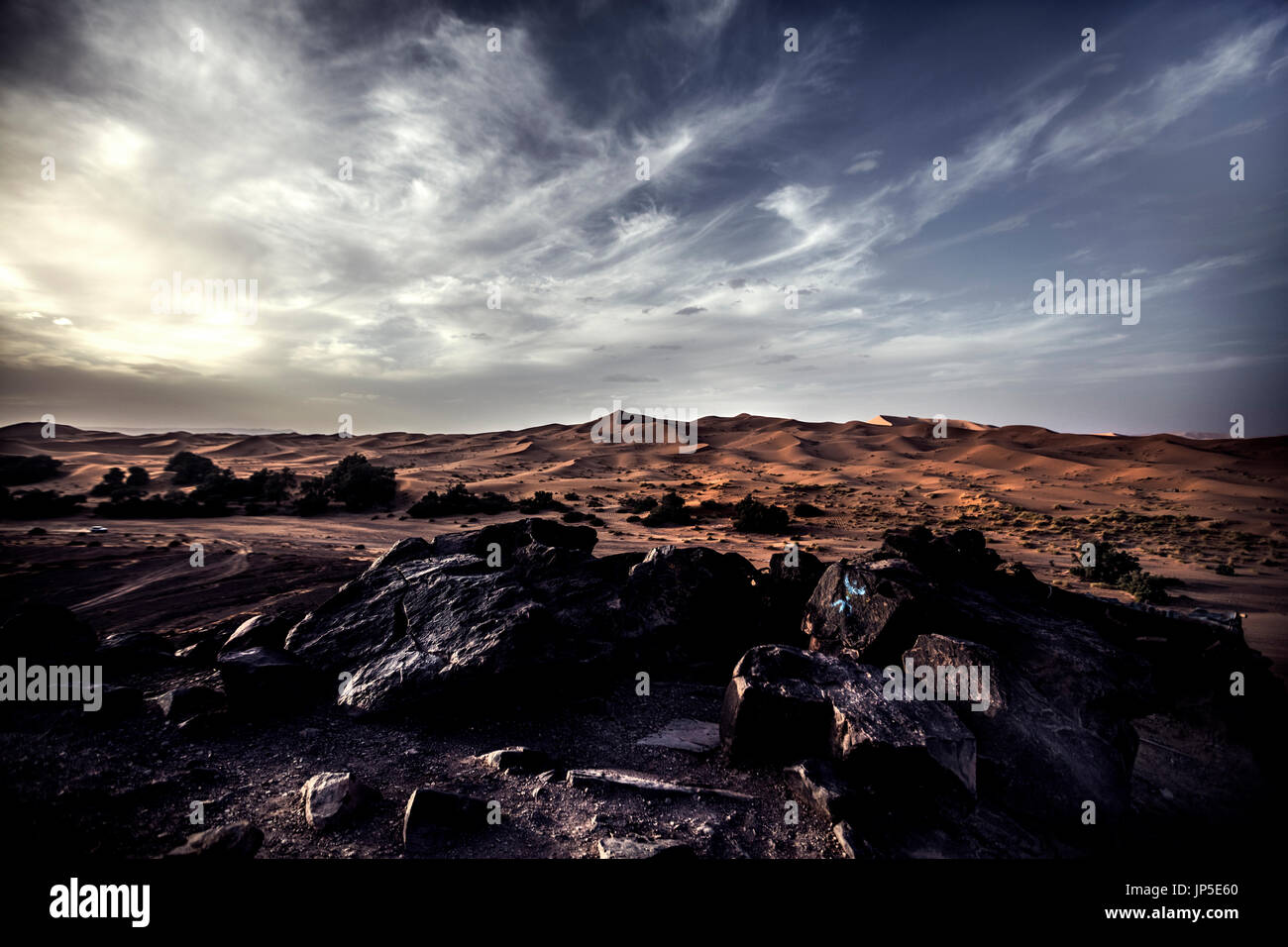 Rocky desert landscape with distant sand dunes under a cloudy sky Stock ...