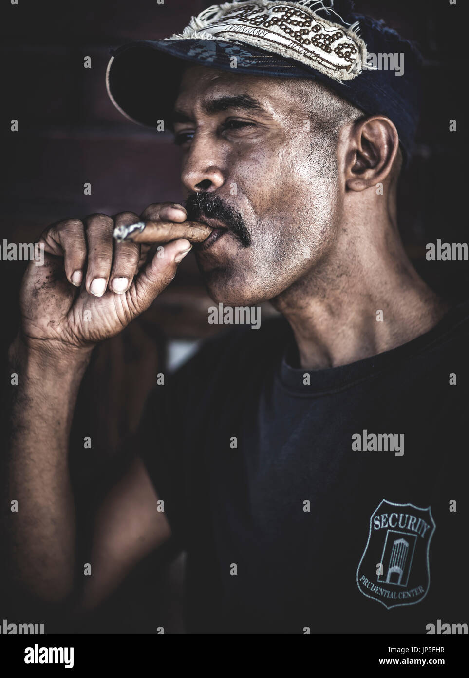 A man wearing a baseball cap smoking a cigar Stock Photo - Alamy