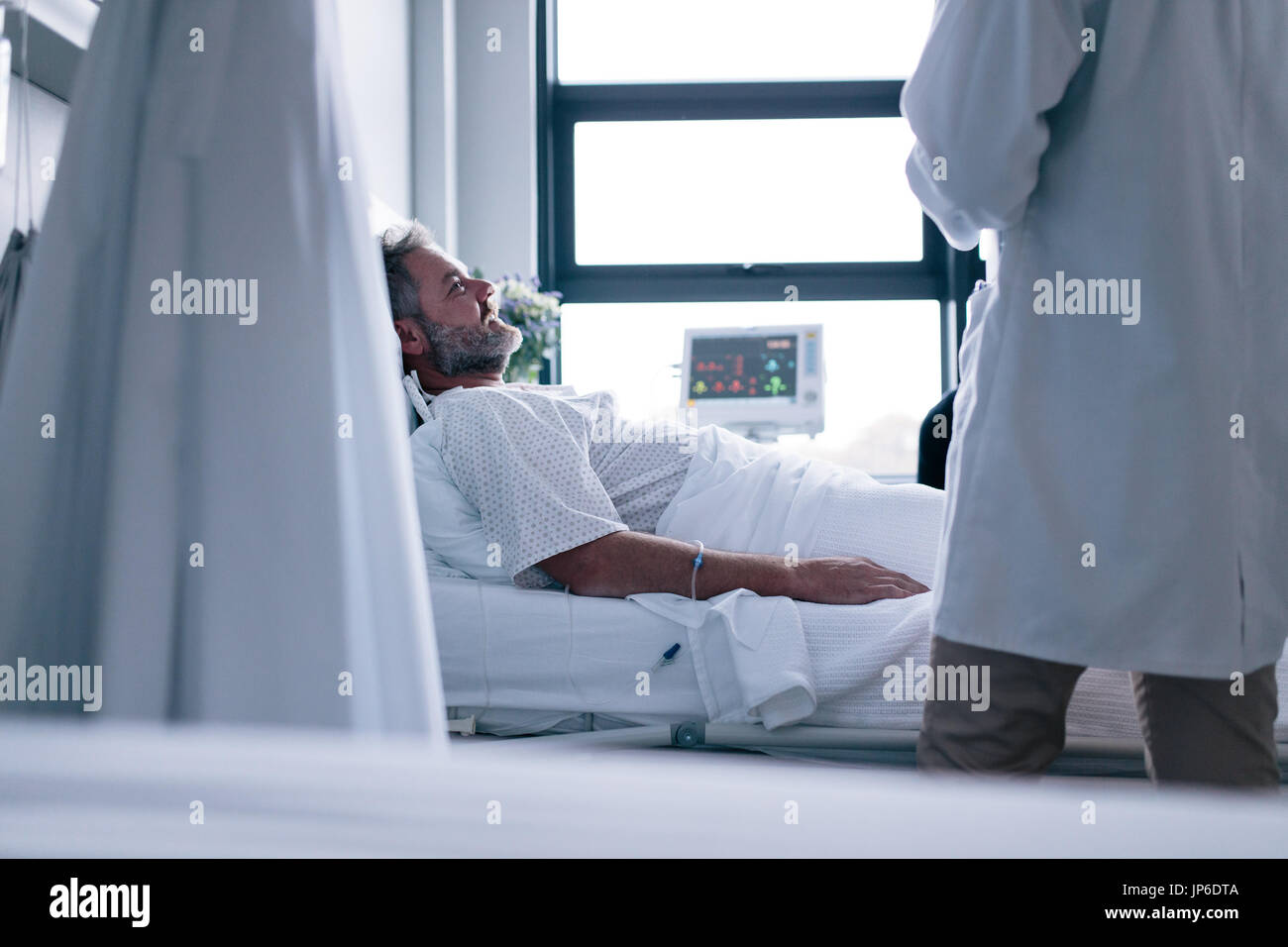 Sick man lying in hospital bed with doctor. Male patient getting ...