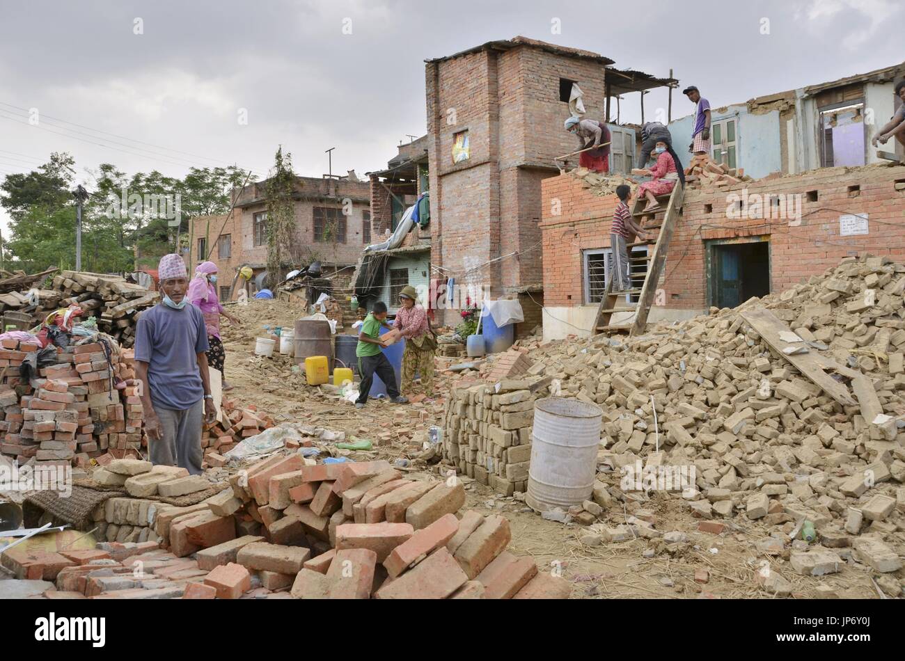 A Nepalese man (L) and his family manually clean up debris at their ...