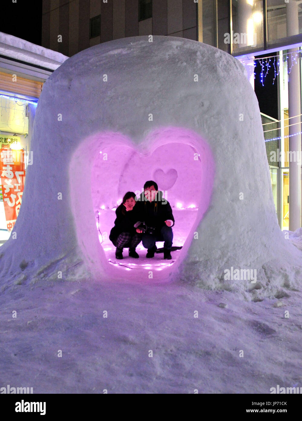 A couple poses for photos inside a snow hut with a heart-shaped ...