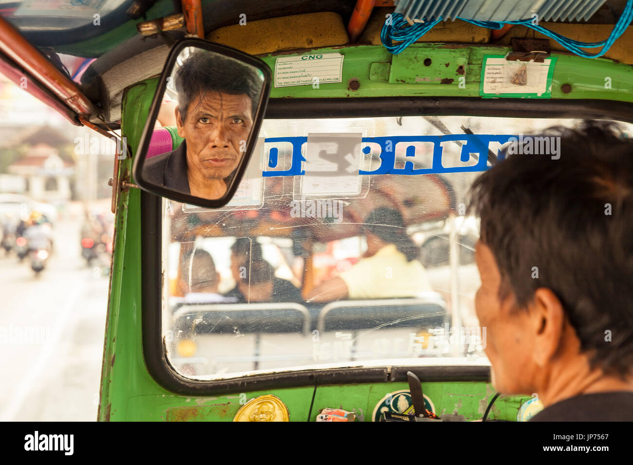 Asian man, driver tuk tuk carefully looks in the rearview mirror ...