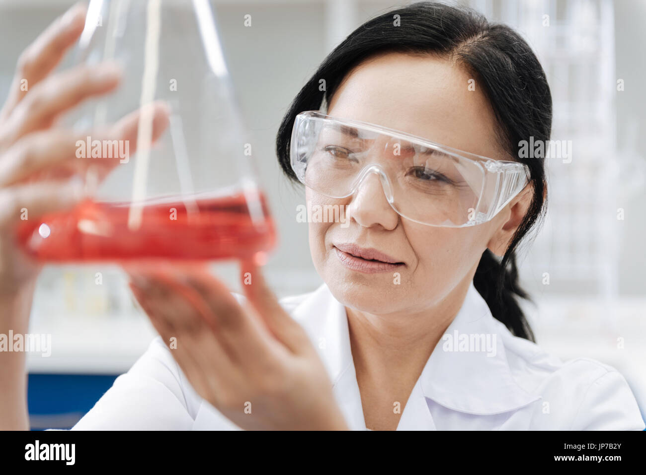 Serious intelligent woman looking at the flask Stock Photo - Alamy