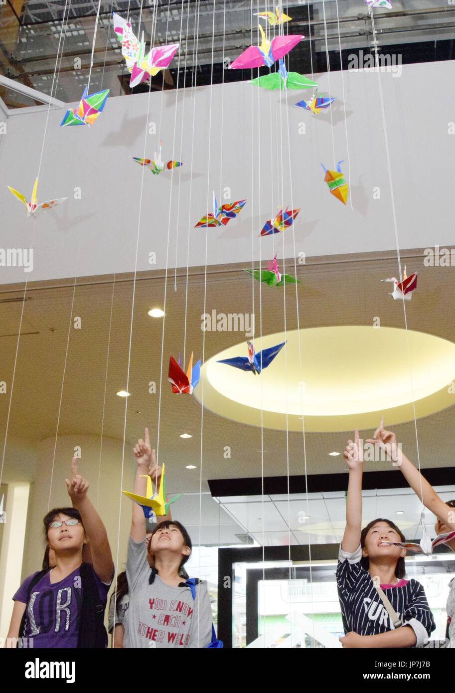 Folded paper cranes of various colors hang from the ceiling at the ...