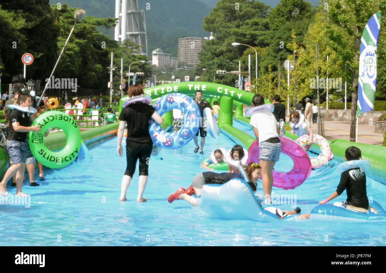 People enjoy a big water slide set up on a public street in the spa ...