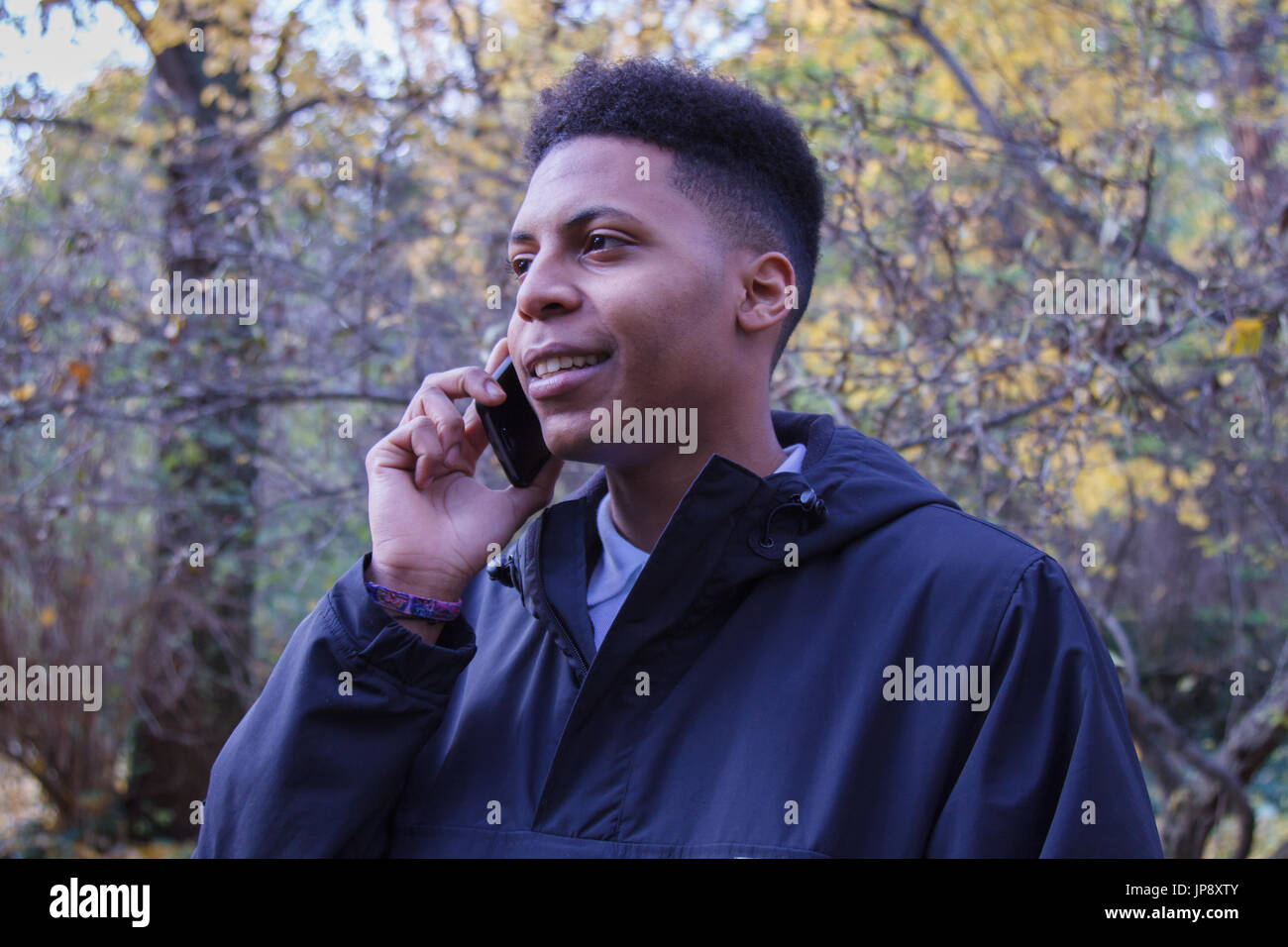 Young black man talking on the phone in the forest. He is laughing ...