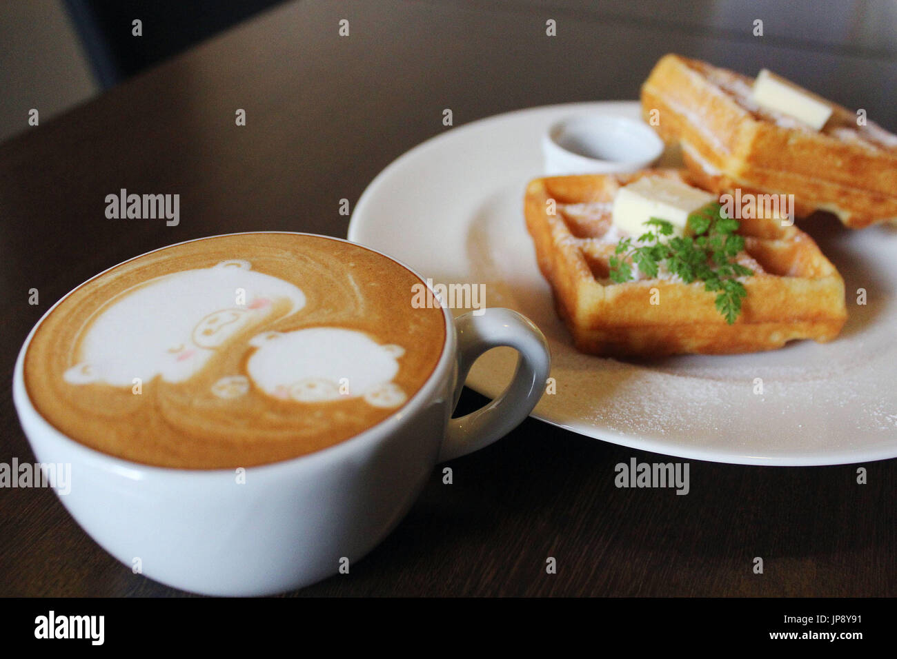 Waffles and a cup of latte decorated with the latte art of a bear are ...