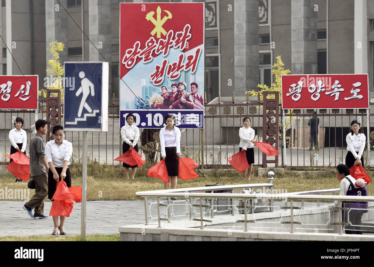 Women wave flags in front of a signboard (C) celebrating the 70th ...
