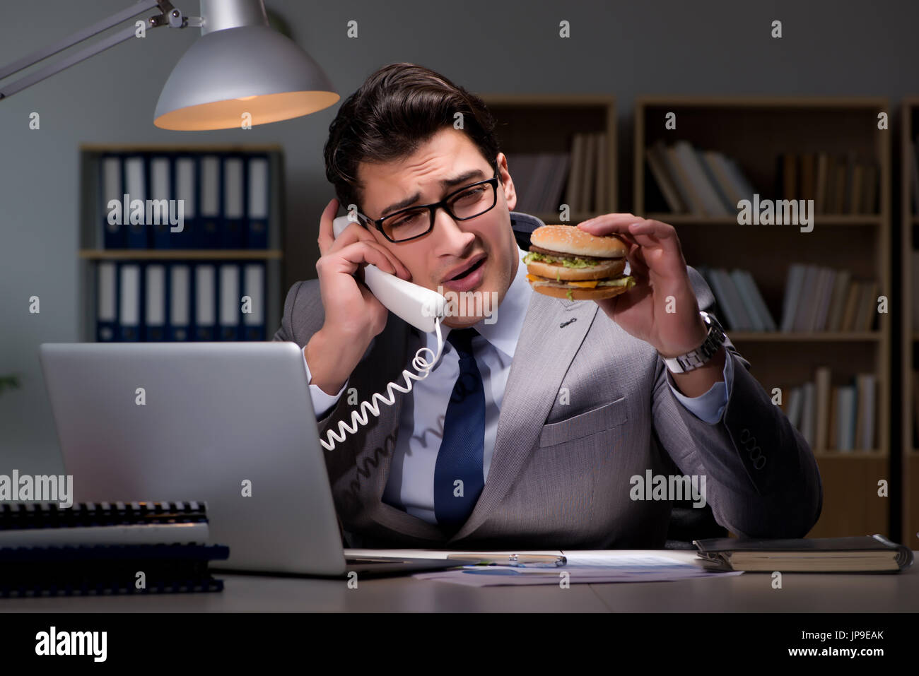 Businessman late at night eating a burger Stock Photo - Alamy