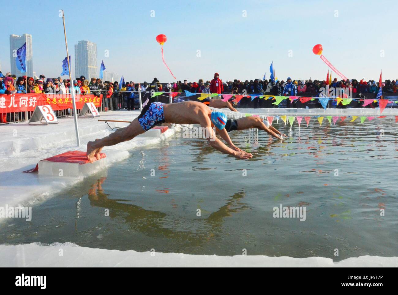 A crowd watches swimmers diving into a hole dug in an ice-covered river ...