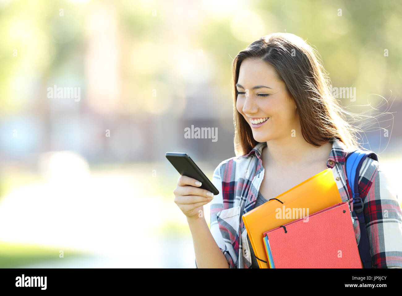Single happy student holding folders walking and using a mobile phone ...