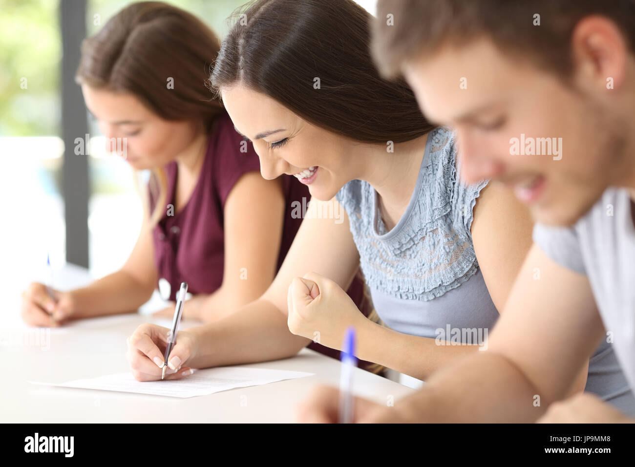 Excited student during an exam at classroom with other classmates in ...