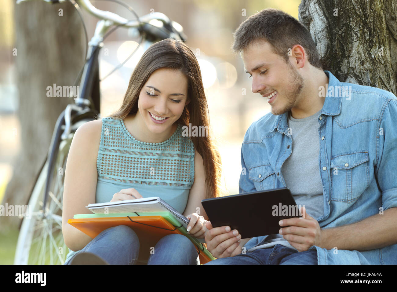 Two happy students learning together on line with a tablet and taking ...