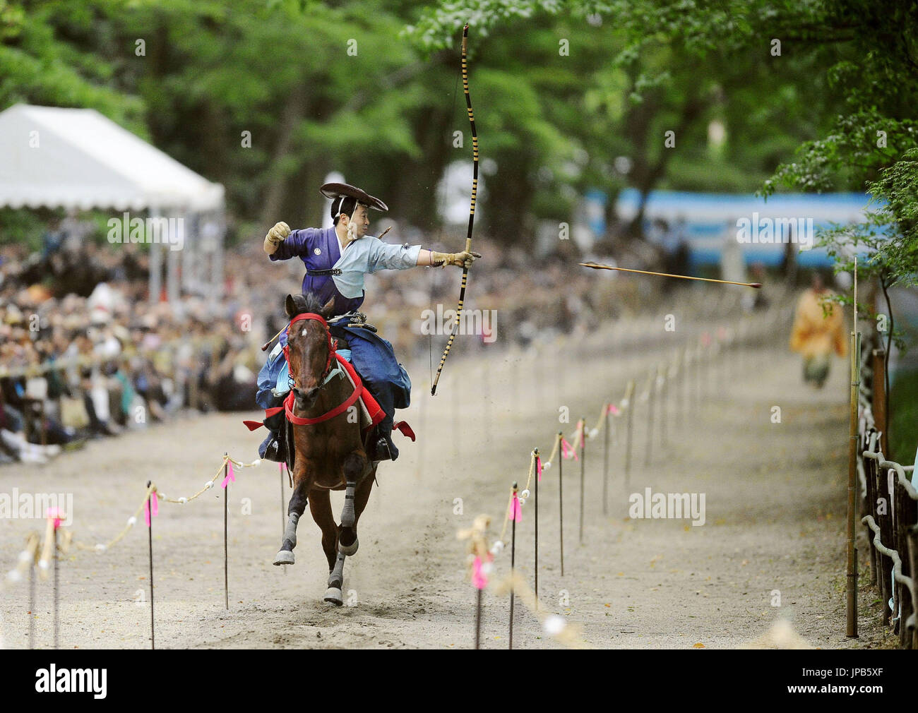 An archer dressed in traditional attire shoots an arrow while riding a ...