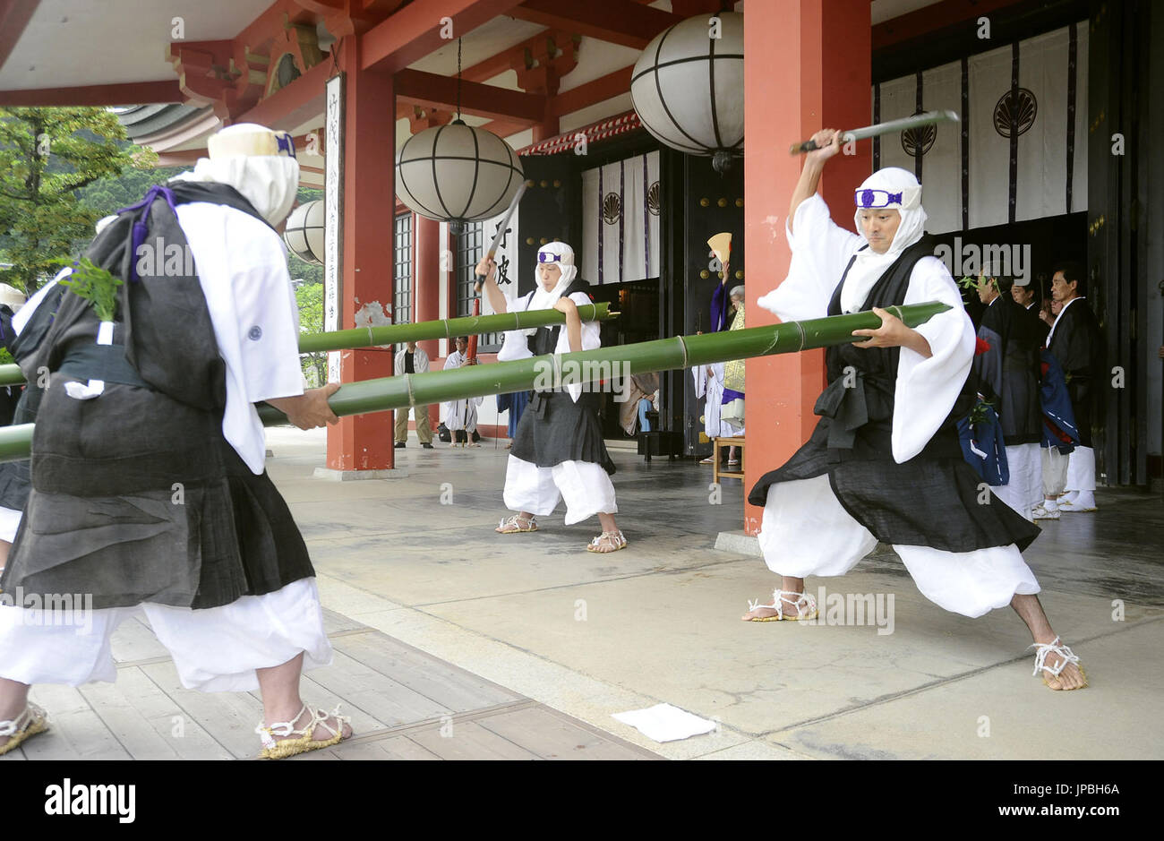 Men dressed as armed priests hack down green bamboo logs, representing ...
