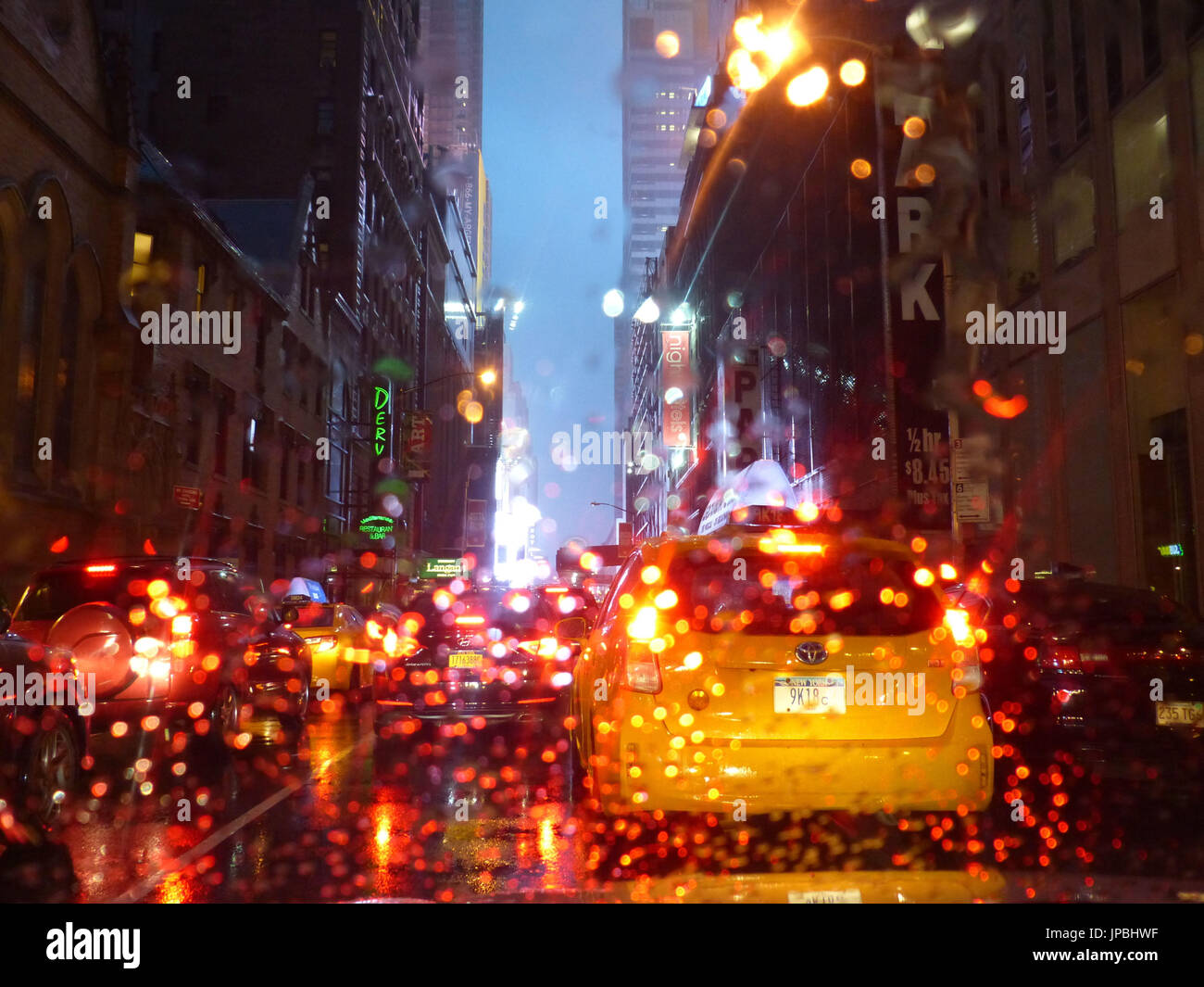 Rain drops on car's windshield are illuminated red by taxicab brake ...