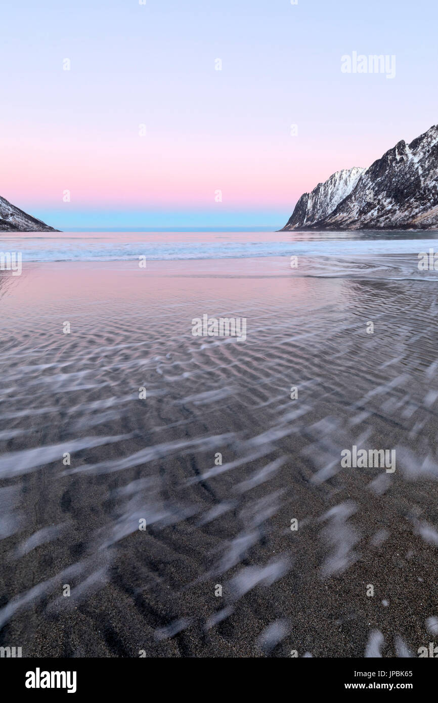 The pink light of sunrise frames the waves of frozen sea surrounded by ...