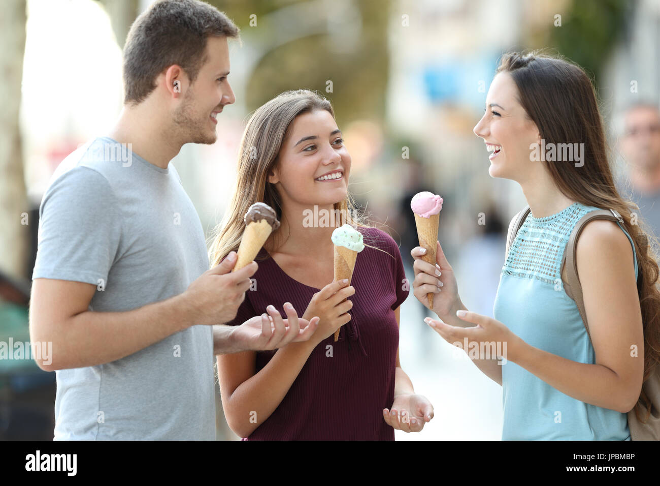 Three happy friends talking and eating ice creams in the street Stock ...