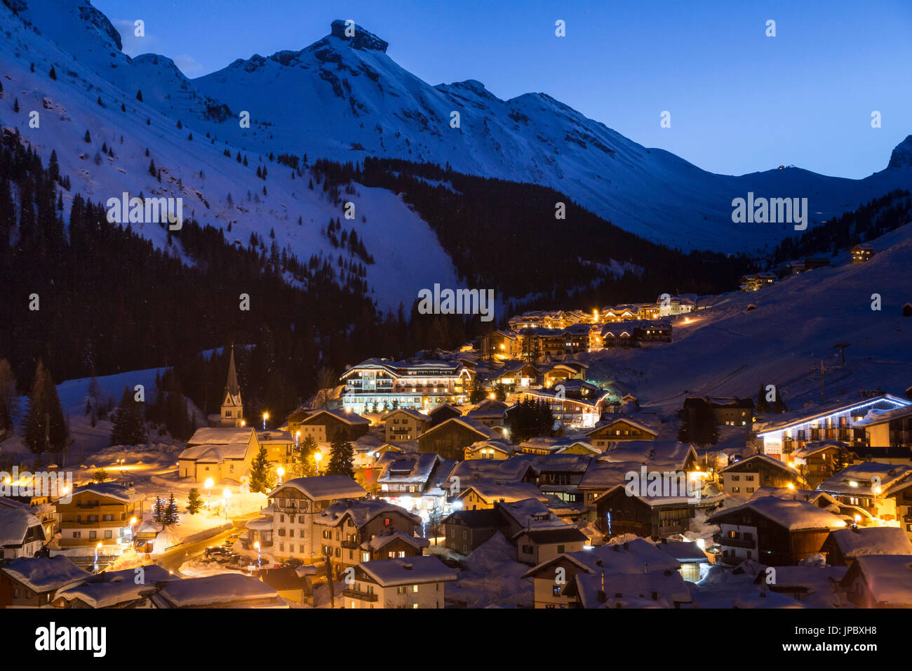 Lights of dusk on the alpine village of Arabba framed by snowy peaks ...