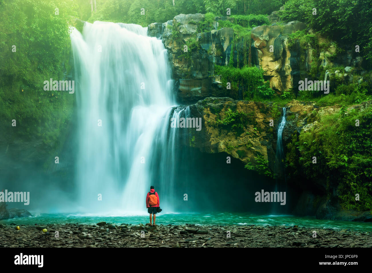 Happy man backpacker enjoying amazing tropical waterfall raised hands ...
