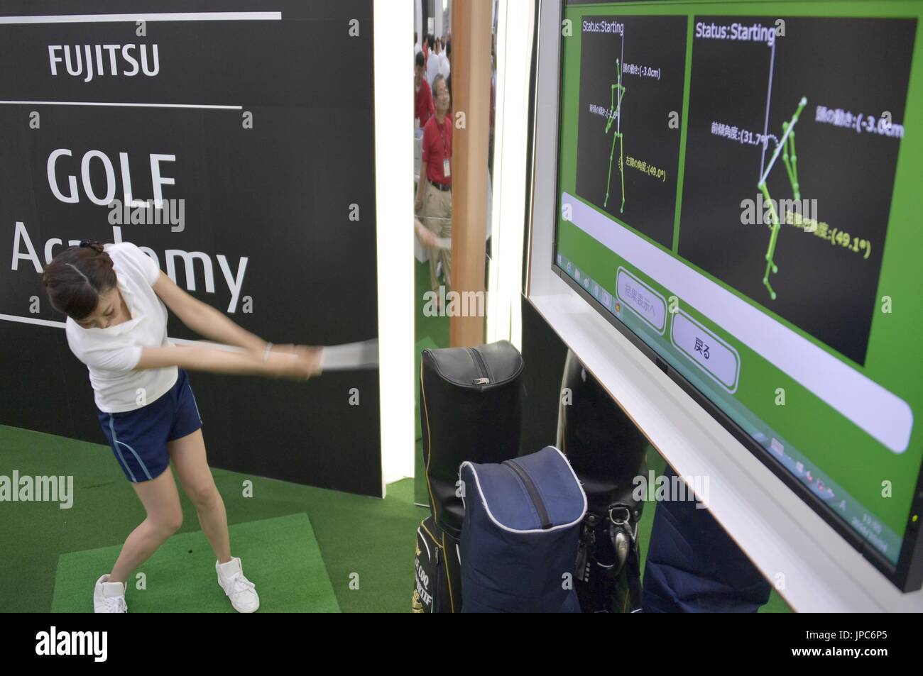 A woman performs a golf swing at Fujitsu Ltd.'s booth at the annual ...