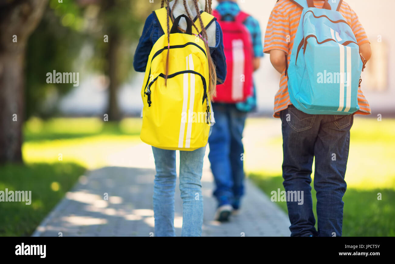 Children with rucksacks standing in the park near school. Pupils with ...