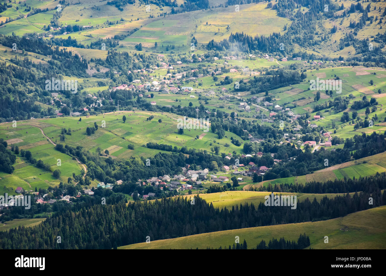 village in sunlit valley view from above. forest with golden foliage on ...