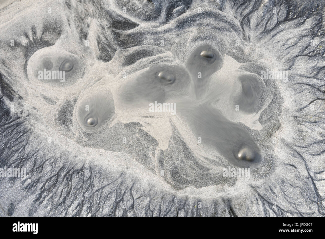 Water oozing out on the surface of a sandy beach forming bizarre shapes ...