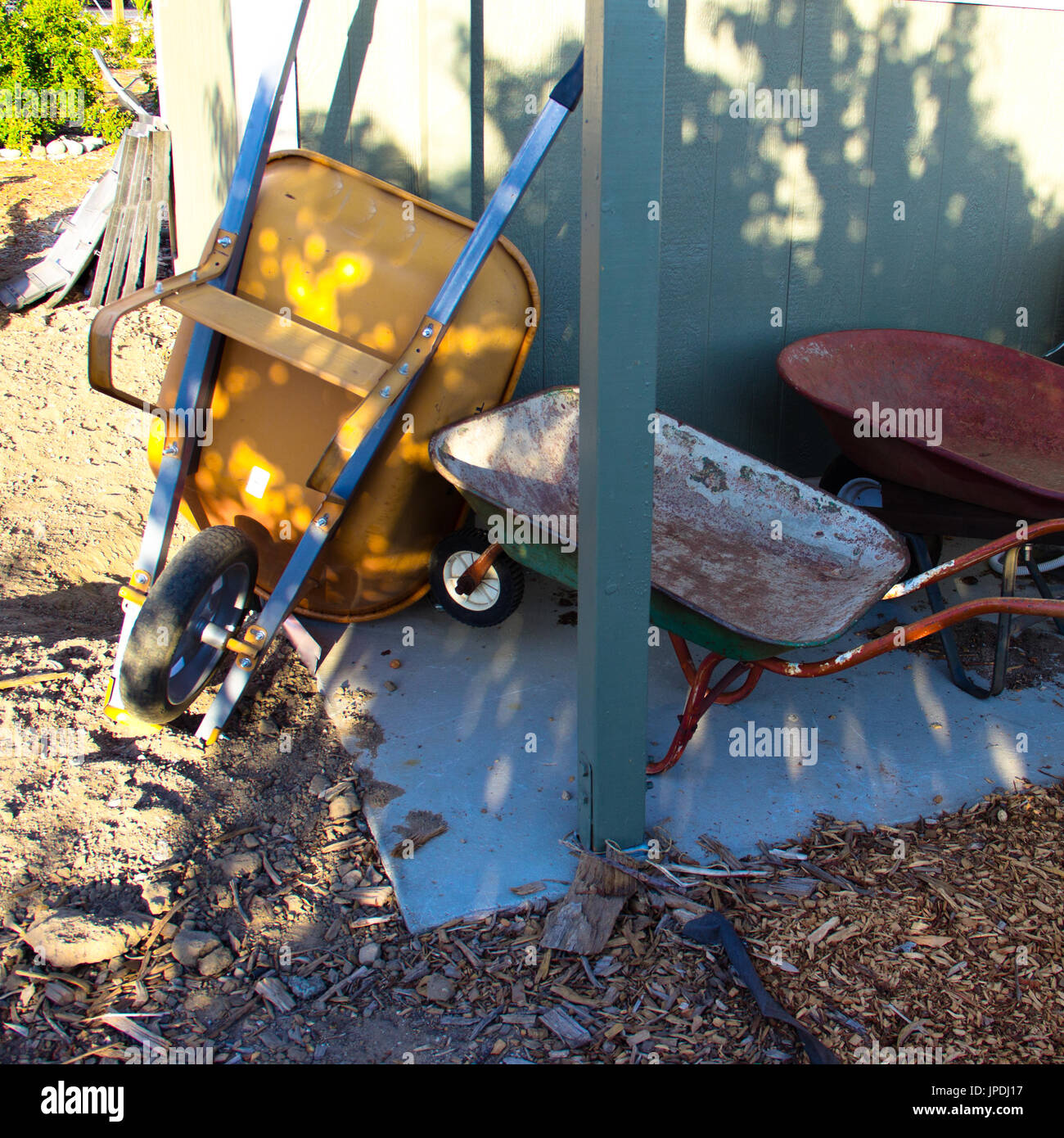 Three well-used wheelbarrows sit stacked against a shady wall Stock ...