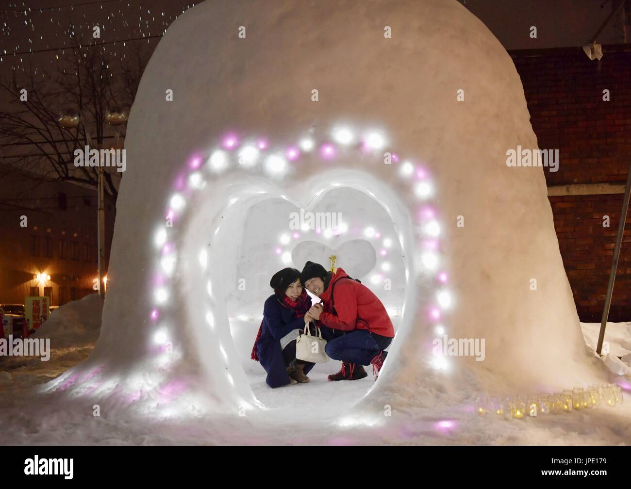 A couple pose inside a snow hut with a heart-shaped entrance, made ...