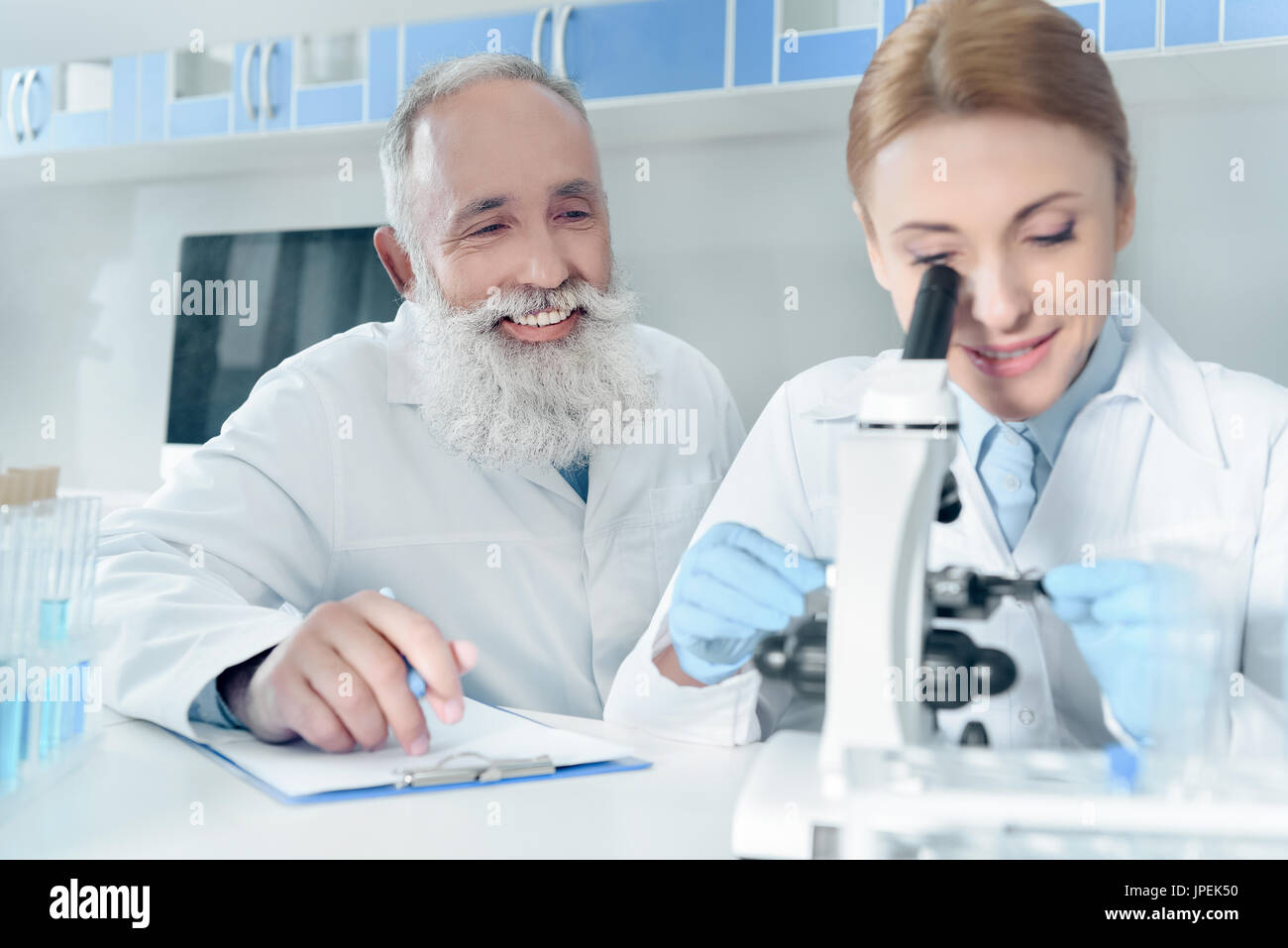 two happy scientists in white coats working together with microscope in chemical laboratory ...