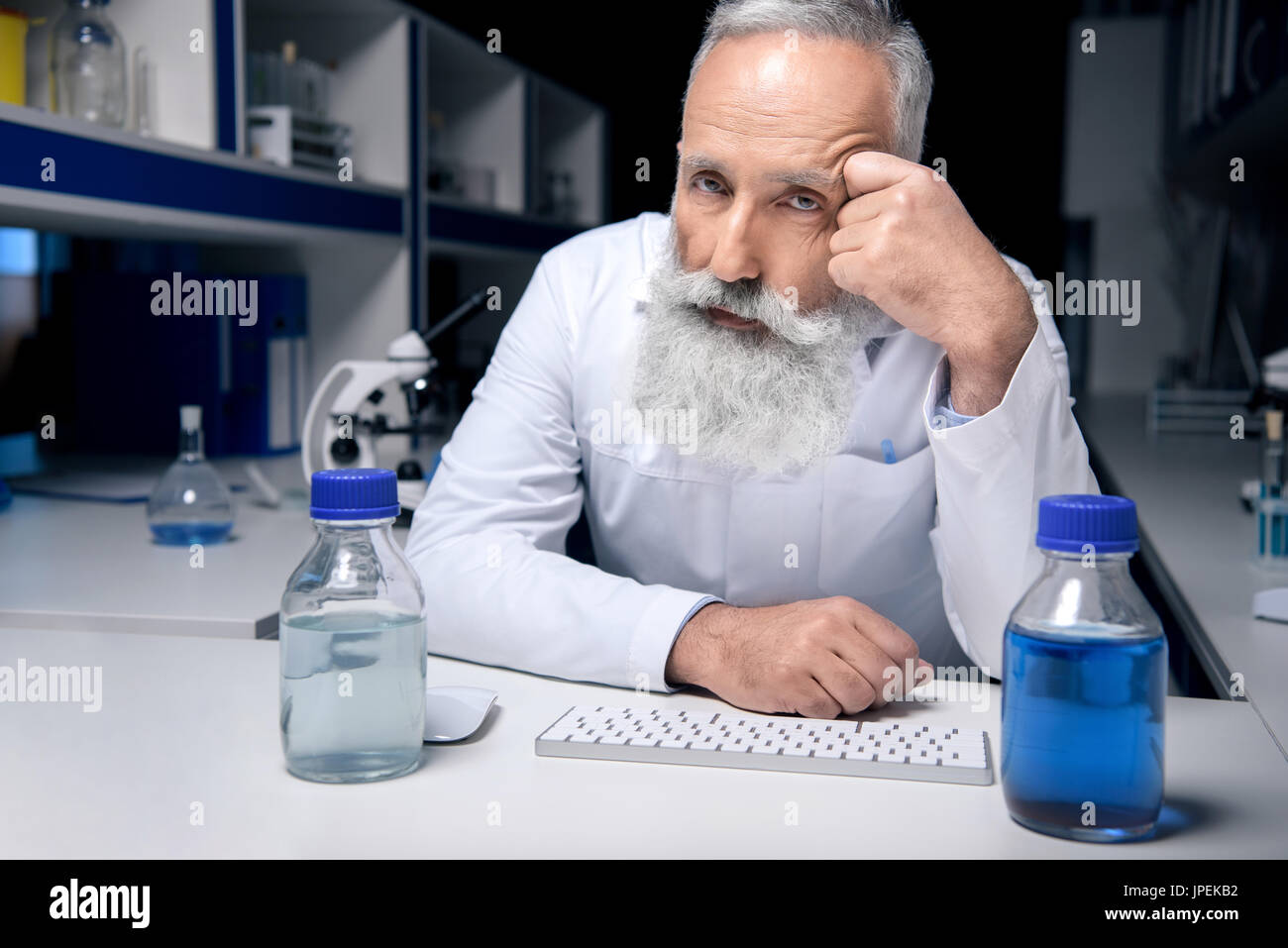 portrait of tired senior scientist sitting at workplace and looking at ...