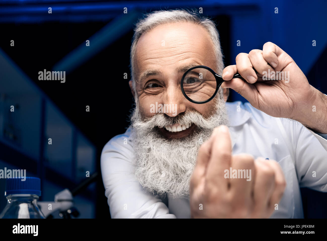 portrait of smiling scientist looking at hand through magnifying glass ...