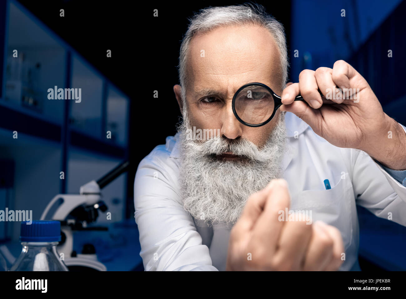 portrait of focused scientist looking at hand through magnifying glass ...
