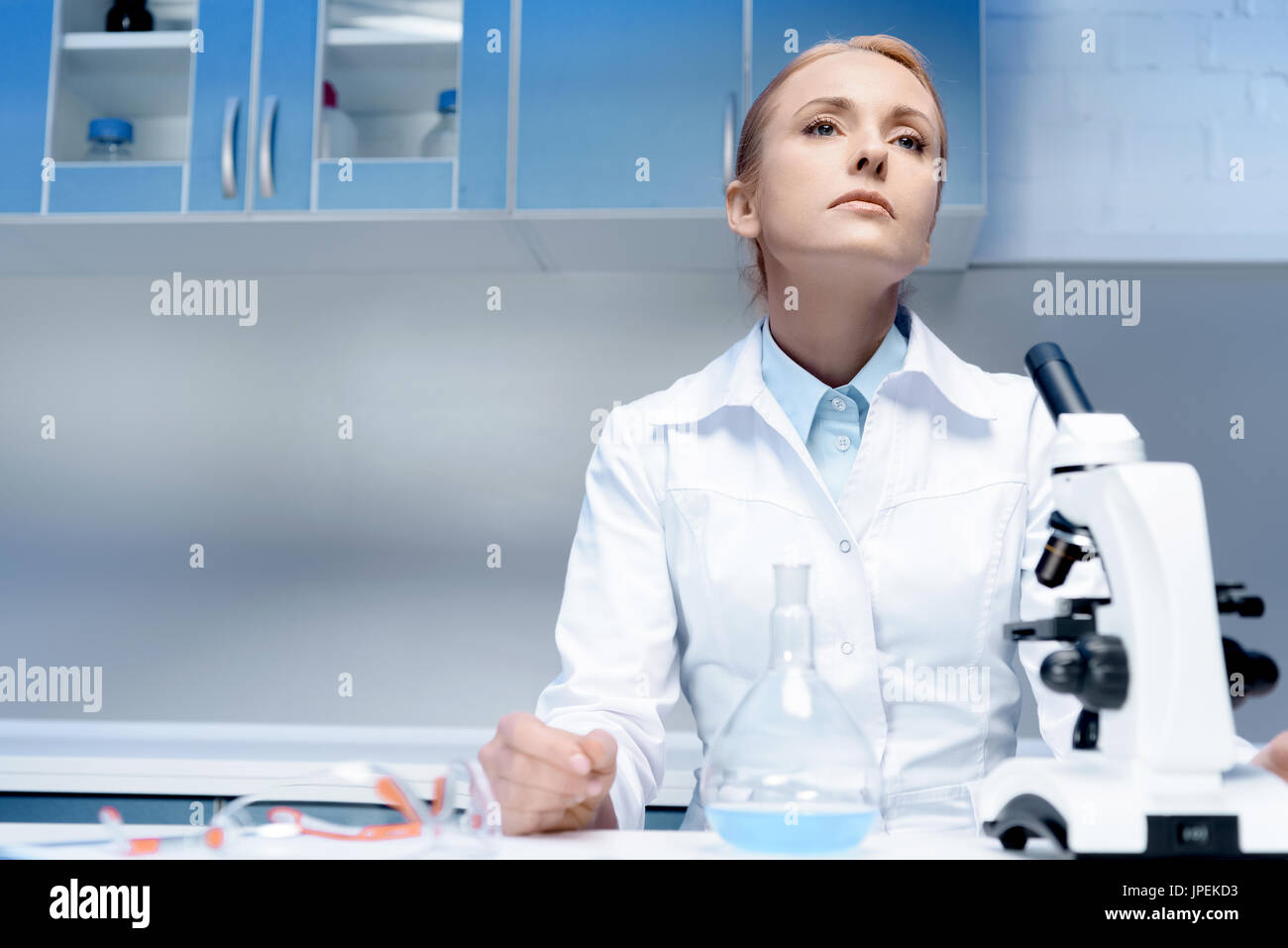 portrait of tired scientist in white coat sitting at workplace in ...