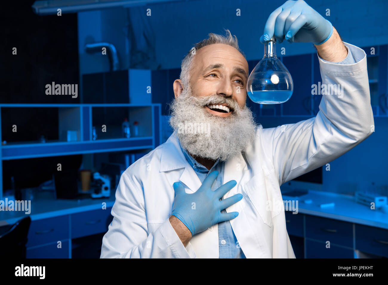 happy grey haired scientist in lab coat holding flask with reagent ...