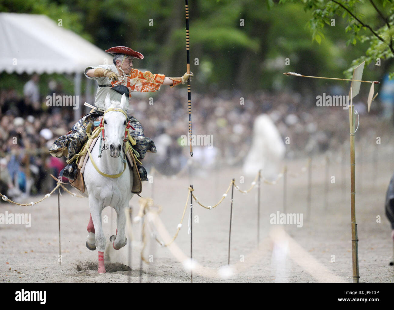 An archer dressed in traditional attire shoots an arrow while riding a ...