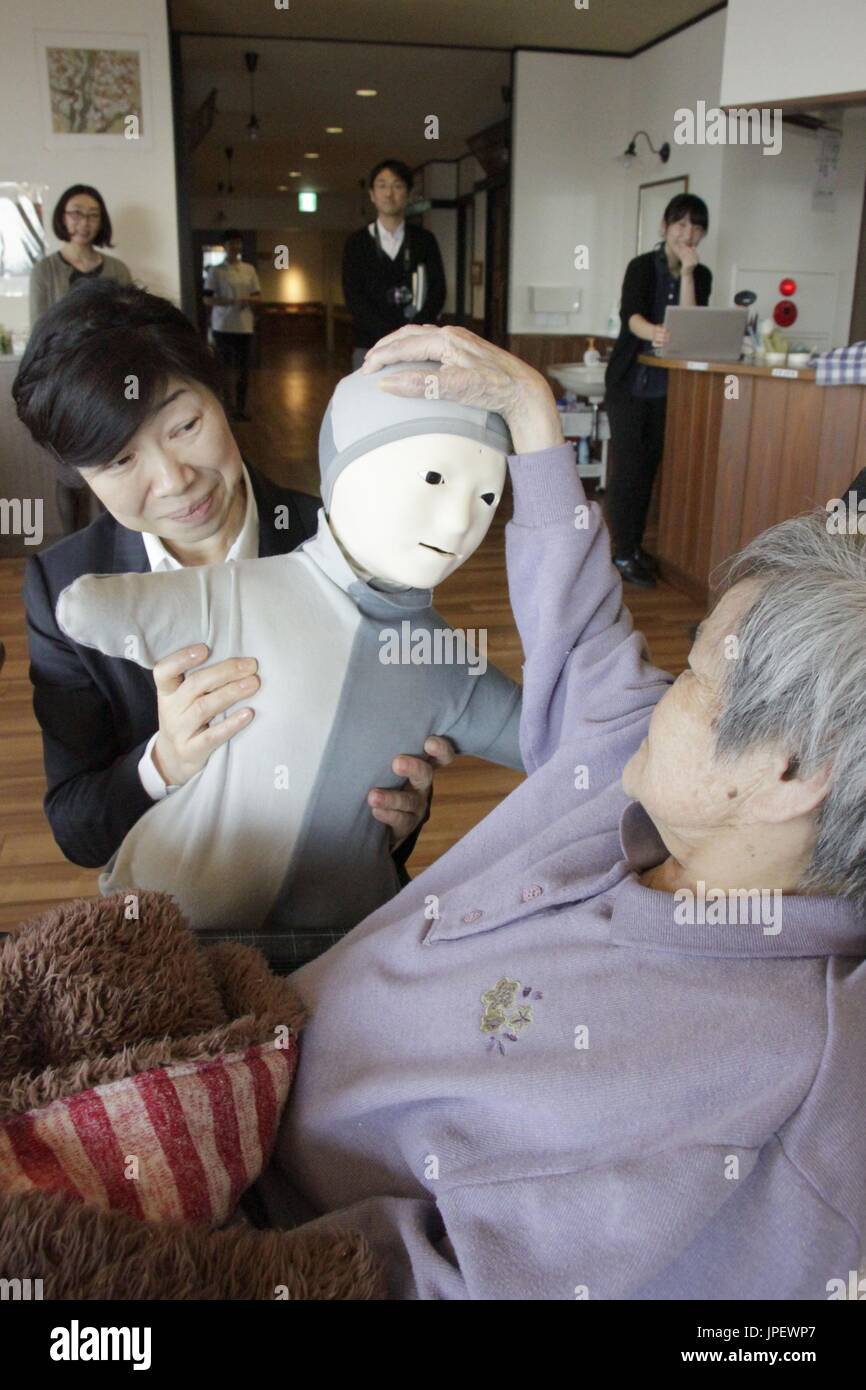 An elderly woman pats a Telenoid robot on the head at a nursing care ...