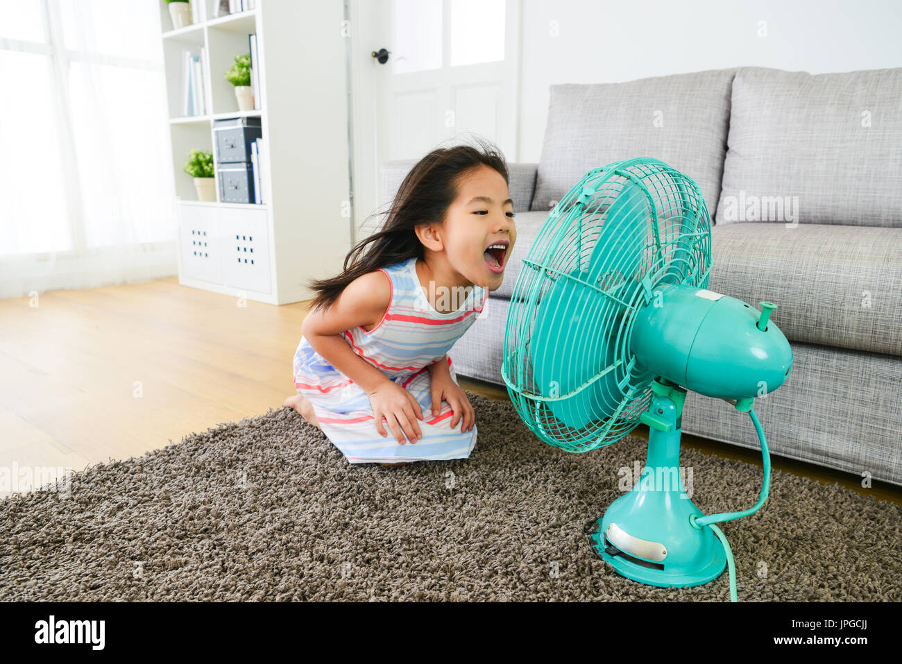 lovely young female children face to electric fan laughing and playing ...