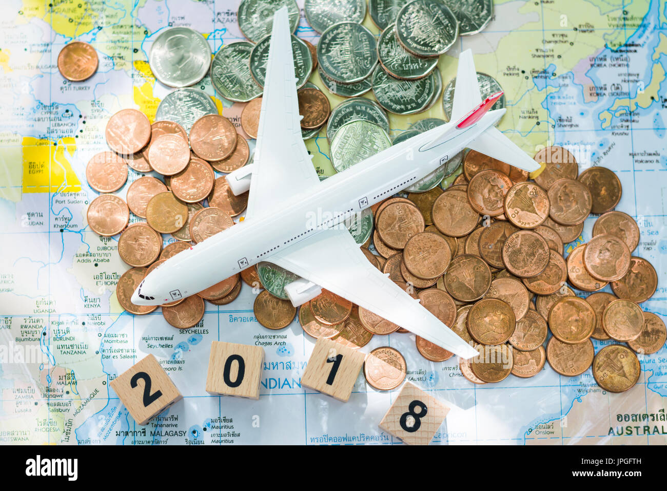Airplane figure on a world map and a pile of coins and wooden numbers ...