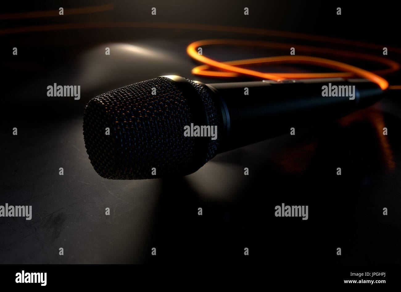 A black metal microphone on laying on a dark stage floor with its cord ...