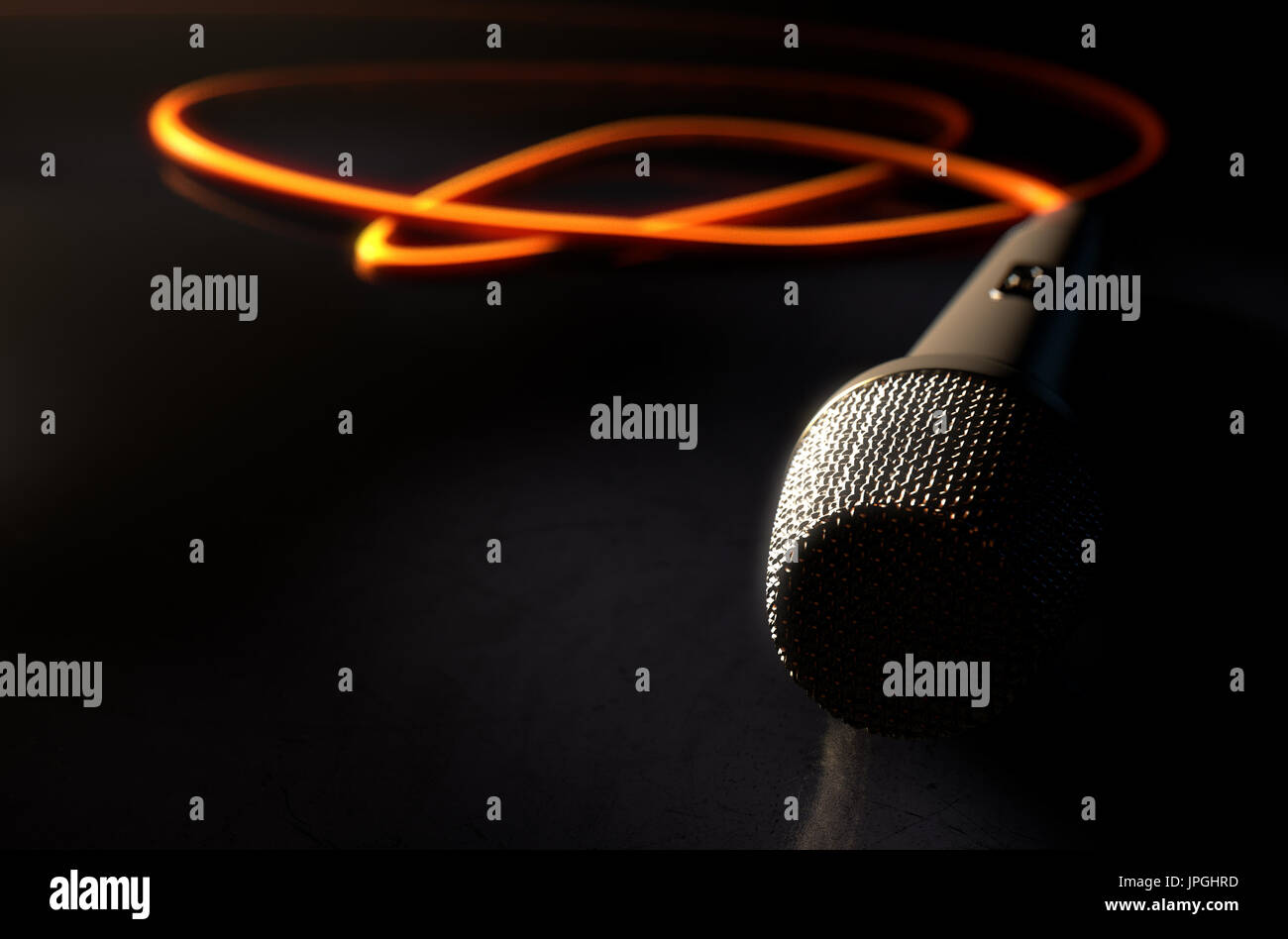 A black metal microphone on laying on a dark stage floor with its cord ...
