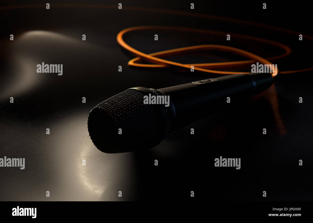 A black metal microphone on laying on a dark stage floor with its cord ...