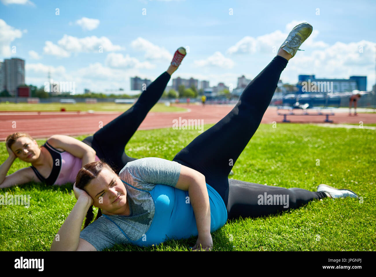 Small group of plus-size females lying on grass and lifting stretched ...